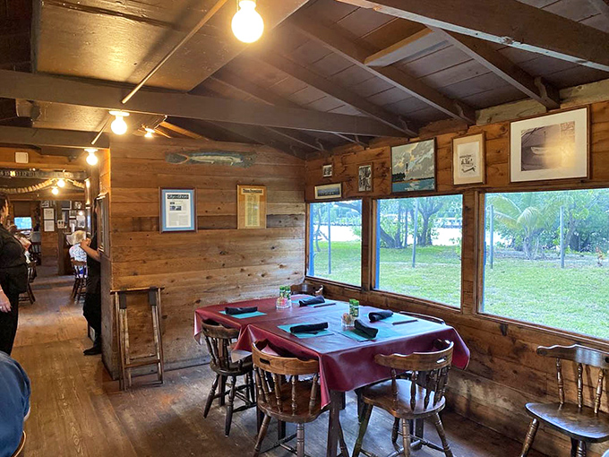 Wooden walls, windows overlooking greenery, and red tablecloths create a dining room that feels like a secret clubhouse for seafood lovers.