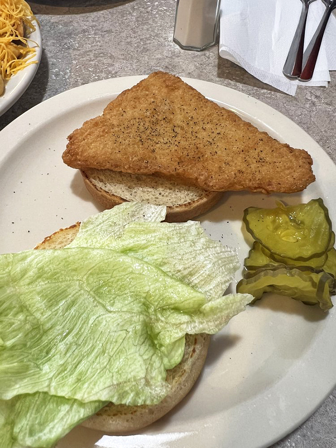 A simple fish sandwich with crisp lettuce and pickle chips – proof that sometimes the classics need no improvement, just proper execution.