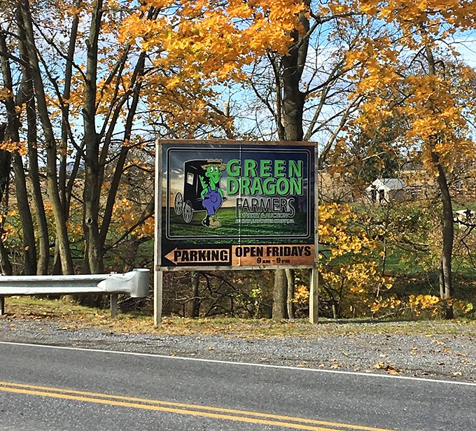 Autumn's golden backdrop frames the market's roadside sign, announcing the weekly Friday ritual that's been drawing crowds since 1932.