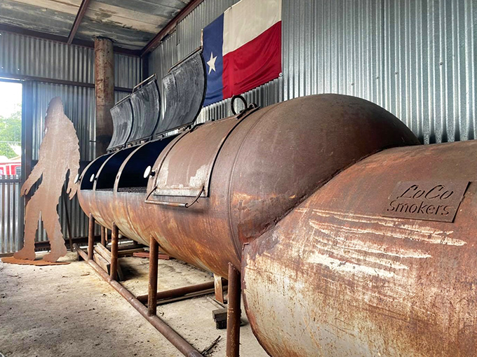 The beating heart of any true barbecue joint: massive smokers flying the Texas flag, where patience transforms tough cuts into tender treasures.