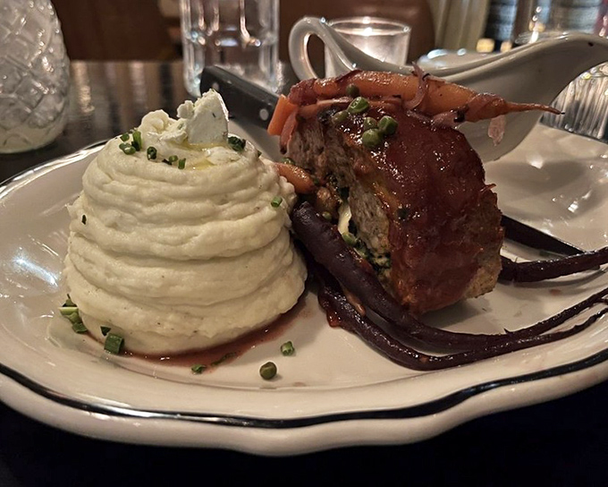 Meatloaf reimagined as the dinner party centerpiece it deserves to be, with mashed potatoes sculpted into a cloud-like mountain beside it.