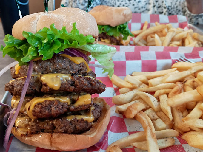 Behold the burger that launched a thousand road trips. Three perfectly seasoned patties stacked higher than your weekend plans, with cheese cascading like a yellow waterfall.