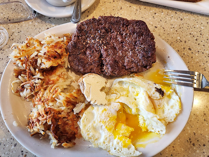 The holy trinity of diner perfection: a juicy burger patty, golden hash browns, and eggs with yolks ready for their close-up.