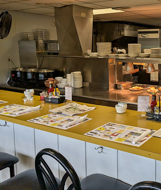 The counter seating offers front-row tickets to the kitchen symphony—newspapers included for those peaceful solo breakfast moments.