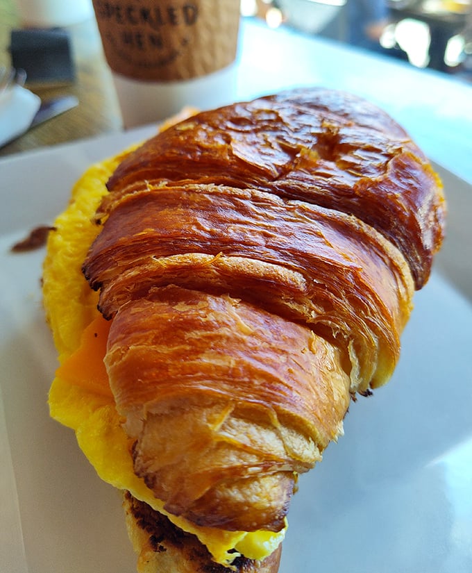 A croissant with serious intentions &ndash; buttery, flaky architecture cradling bright yellow eggs in a breakfast sandwich worth setting alarms for.