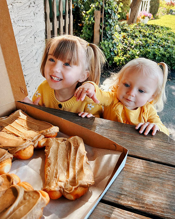 The image shows two young children looking at pastries with the kind of wonder usually reserved for Christmas morning.