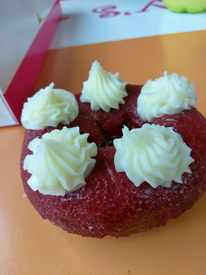 The red velvet donut with cream cheese frosting rosettes looks like it graduated from pastry school with honors.