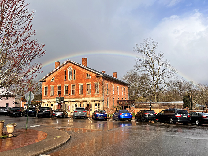 A charming historic brick building stands proudly on a main street, its timeless presence enhanced by a gentle rainbow arching across the sky, capturing the spirit of a town that cherishes its roots.