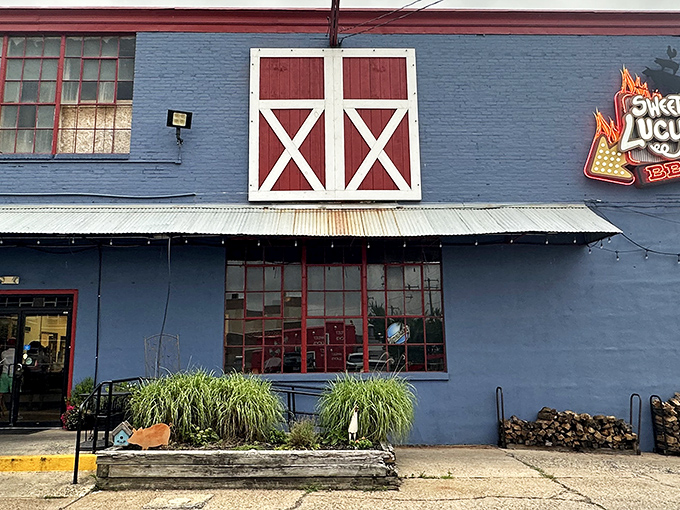 That iconic red barn door against blue siding isn't just rural chic—it's a portal to barbecue nirvana. The stacked firewood hints at the serious smoking happening within.