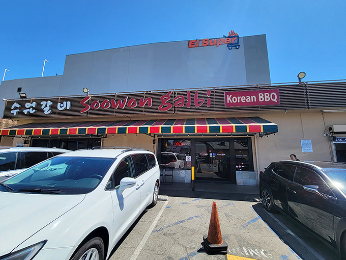 The vibrant red sign of Soowon Galbi beckons like a culinary lighthouse in Koreatown, promising charcoal-kissed delights beneath that cheerful striped awning.