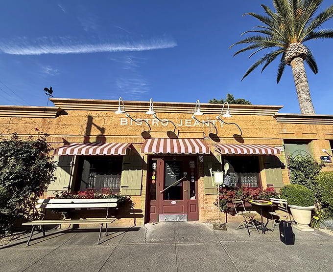 The honey-colored exterior of Bistro Jeanty, with its red-and-white striped awnings and rooster weathervane, promises authentic French charm before you even step inside.