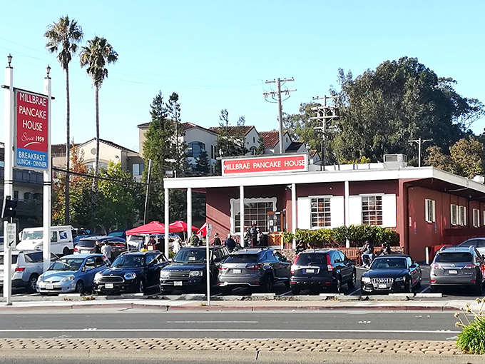 The iconic red exterior of Millbrae Pancake House stands like a beacon of breakfast hope, with cars parked out front as if everyone&rsquo;s stopping by for pancakes.