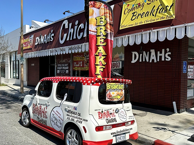 The iconic red and white exterior of Dinah's Chicken beckons hungry travelers like a lighthouse for the famished. Their breakfast flag waves proudly, promising morning delights alongside their famous fried chicken.
