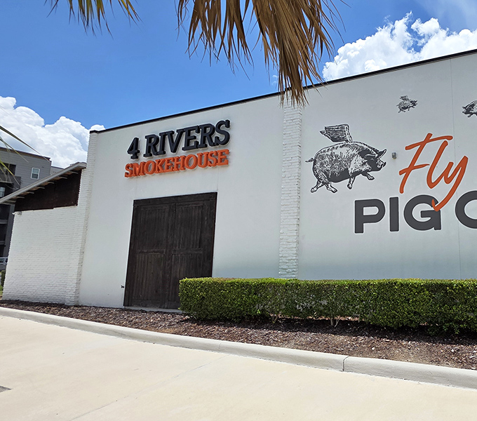 The white brick exterior of 4 Rivers Smokehouse stands like a beacon of barbecue hope, its iconic "4R" logo promising smoky delights within.