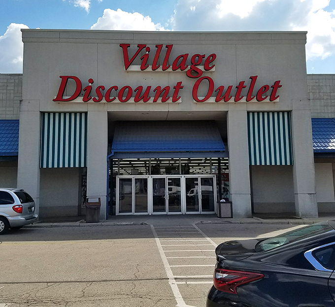 The iconic red lettering of Village Discount Outlet beckons bargain hunters like a retail lighthouse guiding ships to treasure-filled shores.