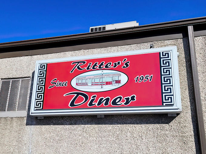 The iconic red sign beckons like a lighthouse for hungry souls. Ritter's Diner's mid-century exterior promises comfort food salvation at any hour.