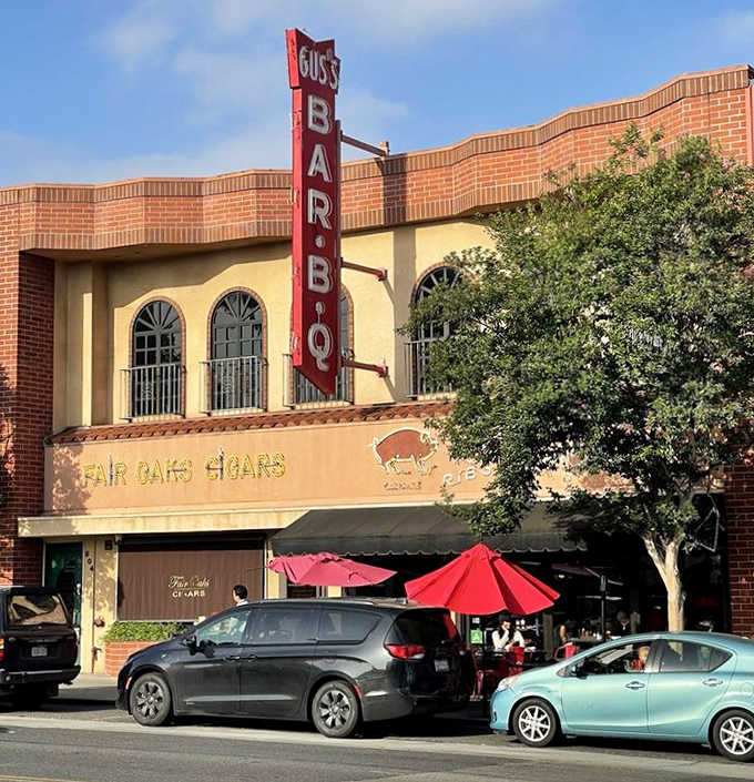 The iconic red vertical sign of Gus's BBQ stands tall against South Pasadena's blue sky, beckoning hungry travelers like a smoky lighthouse for barbecue pilgrims.