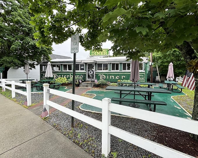 The emerald green exterior of Peterborough Diner beckons like a time machine disguised as a railroad car, complete with patriotic planters guarding the entrance.
