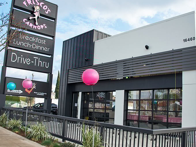 The pink and blue signage of Frisco's stands tall against the California sky, promising retro delights with modern flair. A balloon adds a touch of whimsy.