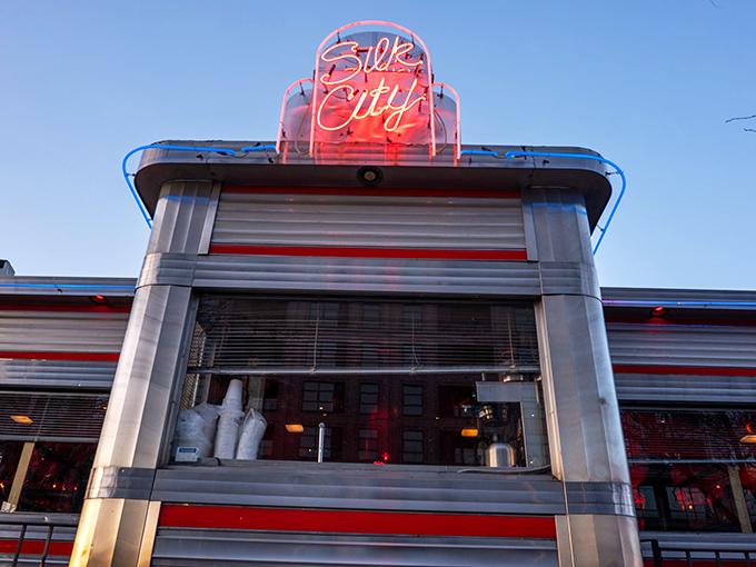 Silk City's iconic neon sign glows like a beacon for hungry night owls, promising retro charm and modern flavors beneath its classic diner exterior.