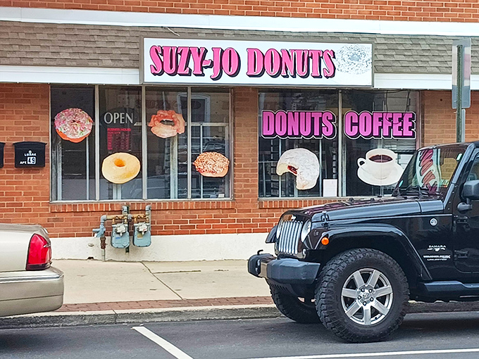 The iconic pink signage of Suzy-Jo Donuts beckons from the brick storefront like a beacon of sugary hope in a world that desperately needs more frosting.