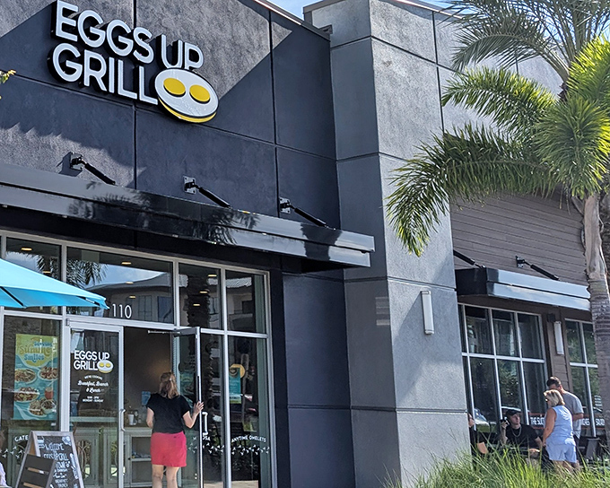 The sleek black exterior of Eggs Up Grill belies the breakfast wonderland within. That cheerful yellow logo is basically a bat signal for pancake enthusiasts.