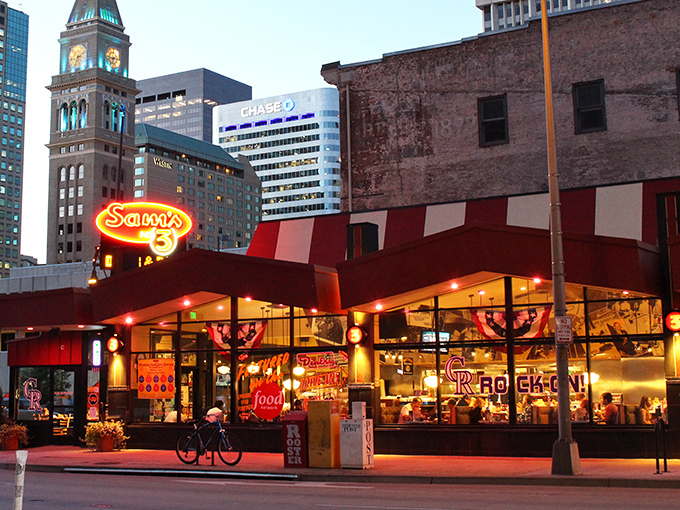 Sam's iconic neon sign glows against Denver's skyline like a beacon for hungry souls. The red-and-white awning promises comfort food salvation in the heart of downtown.
