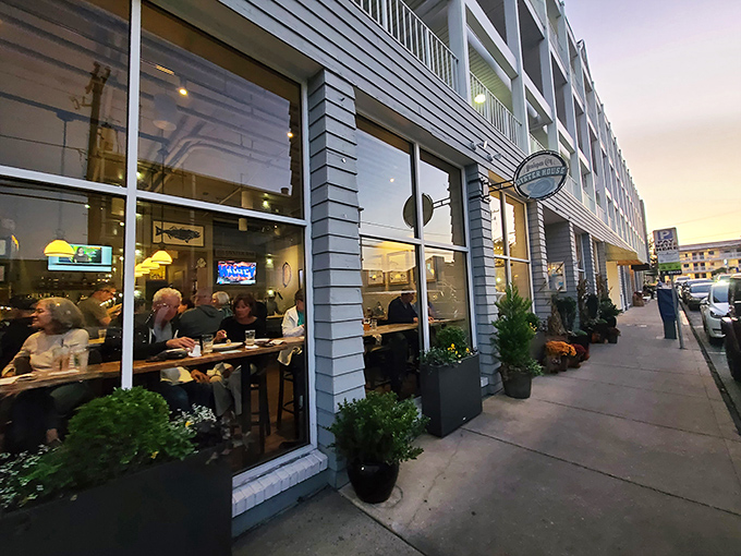 The blue-gray exterior of Henlopen City Oyster House beckons hungry passersby with its warm glow and lively atmosphere at dusk.