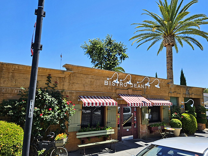 The honey-colored exterior of Bistro Jeanty, with its red-and-white striped awnings and rooster weathervane, promises authentic French charm before you even step inside.