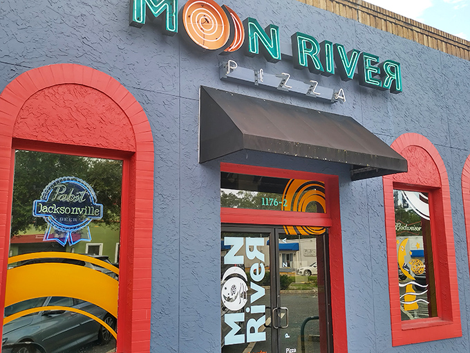 The blue exterior with vibrant neon signage announces you've arrived somewhere special. Moon River's fa&ccedil;ade promises a colorful pizza adventure inside.