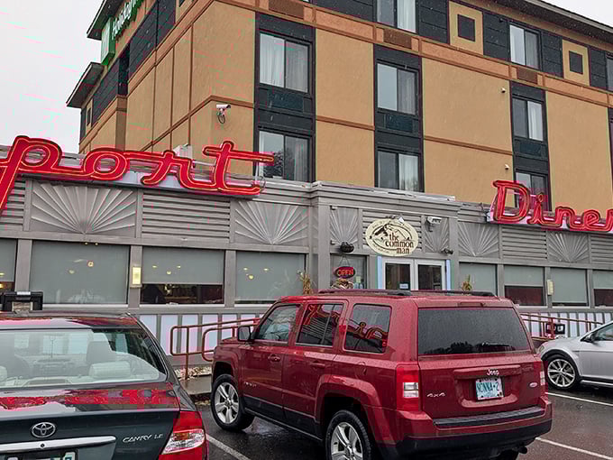 The iconic red neon sign beckons hungry travelers like a culinary lighthouse. The Airport Diner promises comfort food salvation attached to the Holiday Inn.