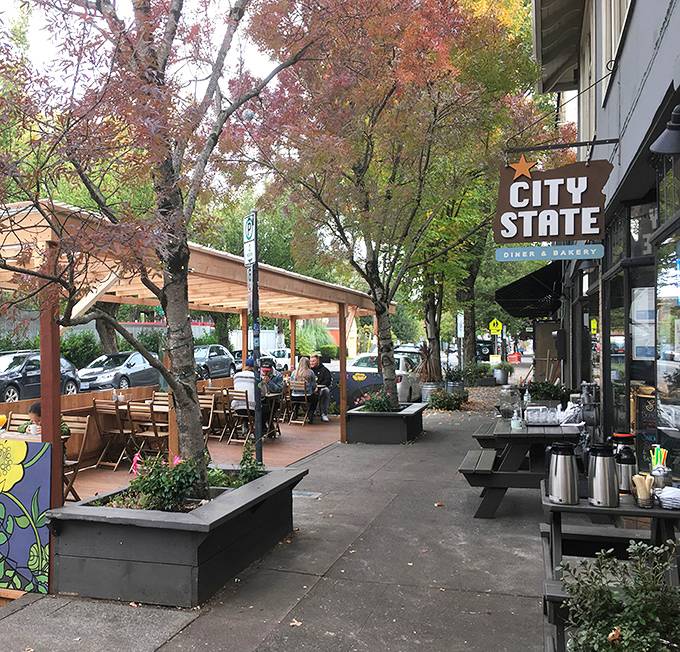 The iconic Oregon-shaped sign welcomes hungry pilgrims to City State Diner & Bakery, where Portland's breakfast dreams come true beneath those towering trees.