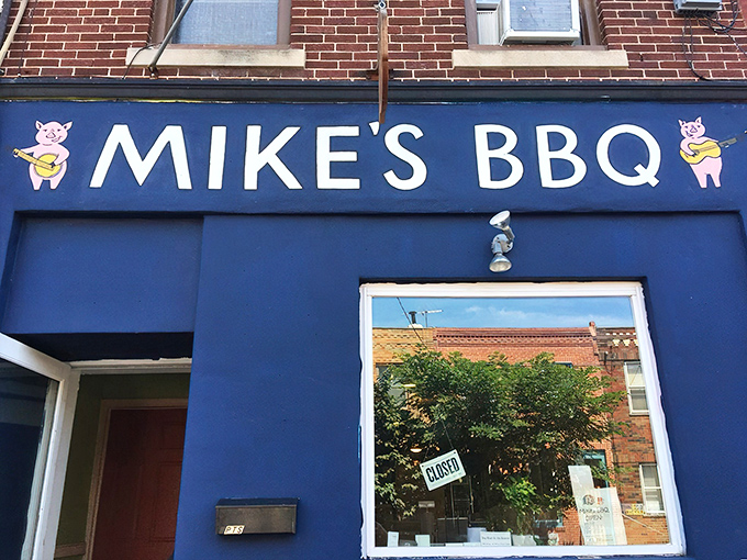 The bright blue storefront of Mike's BBQ stands out like a beacon for meat lovers, complete with adorable cartoon pig mascots playing banjos.