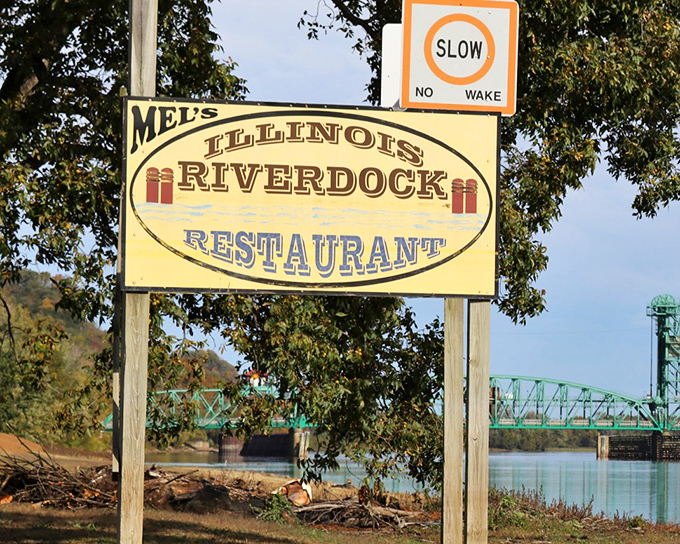 The iconic yellow sign for Mel's Illinois Riverdock Restaurant stands sentinel by the water, promising riverside dining and that famous catfish just beyond the bridge.