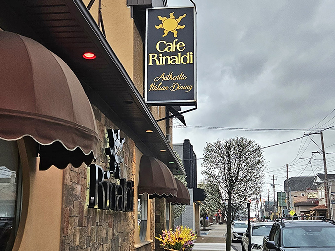 The welcoming fa&ccedil;ade of Cafe Rinaldi beckons with its stone exterior and distinctive burgundy awnings &ndash; Old Forge's culinary beacon on a cloudy Pennsylvania day.