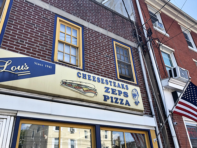 The vintage sign proudly announces Lou's specialties against the brick backdrop. That cartoon face knows something you don't&mdash;how good lunch is about to be.