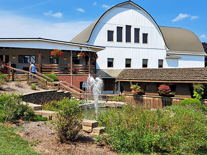 The iconic white barn structure stands proudly against blue Ohio skies, complete with bubbling fountain and colorful flower baskets. Americana at its most inviting!