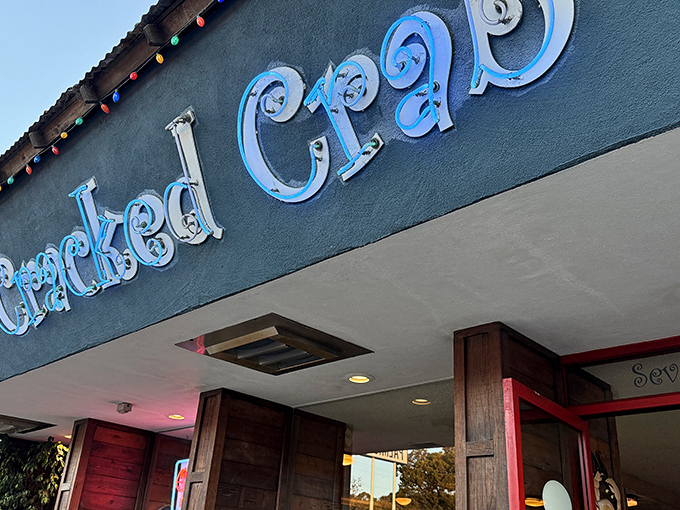 The iconic blue neon sign of Cracked Crab glows like a coastal beacon, promising seafood treasures within. Colorful string lights add a touch of perpetual celebration.