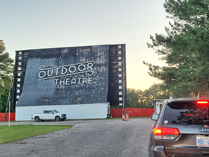 The iconic screen of Raleigh Road Outdoor Theatre stands tall against the sunset, a weathered sentinel of cinema history still proudly serving movie magic.
