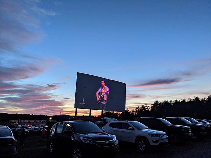 Cars gather under a pastel sunset sky, waiting for darkness to transform this field into a communal theater of dreams and buttery popcorn.