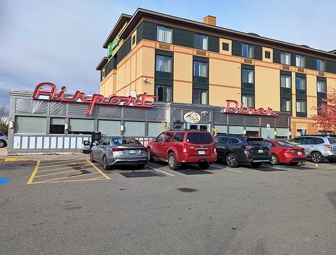 The iconic red neon sign beckons hungry travelers like a culinary lighthouse. The Airport Diner promises comfort food salvation attached to the Holiday Inn.