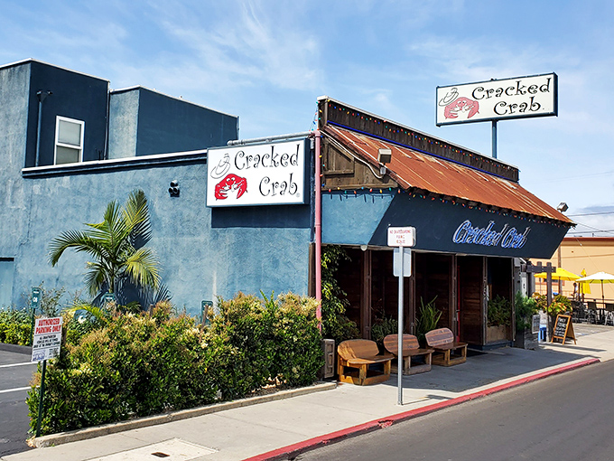 The iconic blue neon sign of Cracked Crab glows like a coastal beacon, promising seafood treasures within. Colorful string lights add a touch of perpetual celebration.