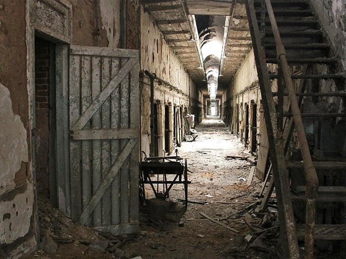 Abandoned corridors stretch into infinity, where peeling paint and rusted cell doors whisper stories of those who once called these narrow passages home.