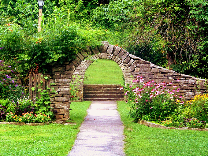 Nature's perfect archway beckons visitors through a limestone portal, where wildflowers stand guard like colorful sentinels.