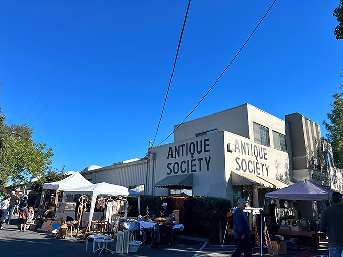 The iconic white facade of Antique Society stands proudly against the California blue sky, with outdoor vendors creating a festive marketplace atmosphere.