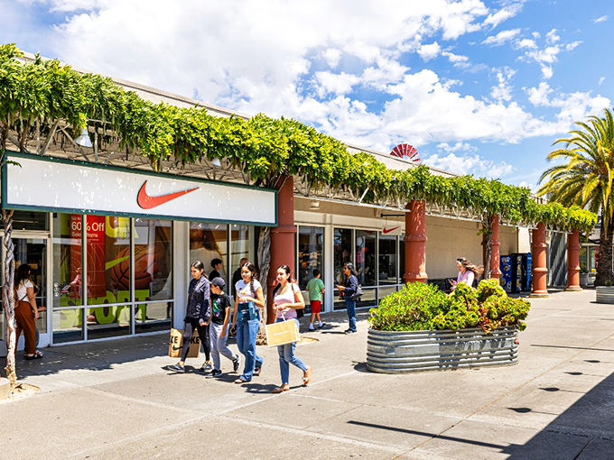 The vine-draped storefronts of Nike and neighboring shops create a California-casual atmosphere where bargain hunting feels less like a mission and more like a Mediterranean holiday.