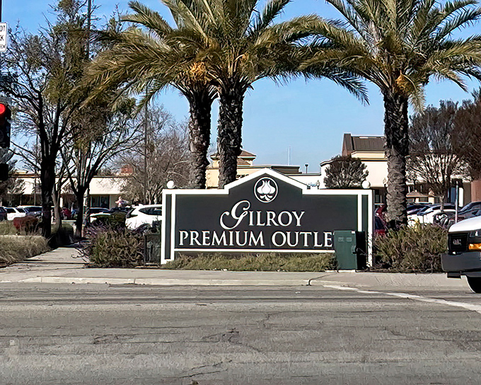 The iconic entrance to Gilroy Premium Outlets, where palm trees stand guard over fashion treasures like sentinels of style with discounted price tags.