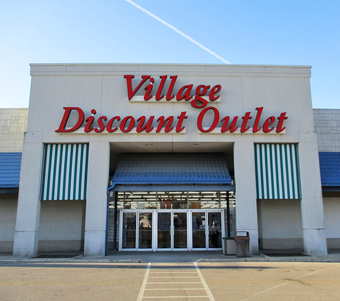The iconic red lettering of Village Discount Outlet beckons bargain hunters like a retail lighthouse guiding ships to treasure-filled shores.