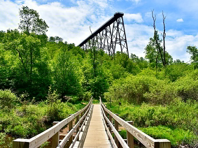 The approach to engineering greatness. A wooden boardwalk leads visitors through lush Pennsylvania greenery toward the towering remains of the once-mighty Kinzua Bridge.