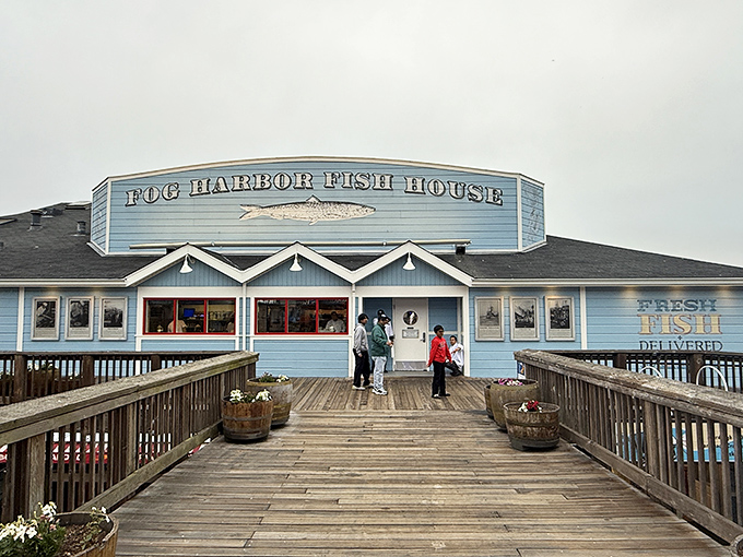 The blue facade of Fog Harbor Fish House welcomes seafood lovers like a maritime beacon, promising oceanic treasures at the end of its wooden boardwalk.